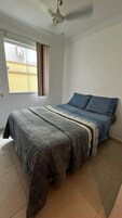 Quarto com cama, ventilador de teto, janela com cortinas e vista para o exterior.