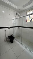 Casa de banho moderna com cabine de chuveiro em vidro, sanita preta e soalho em mosaicos brancos.