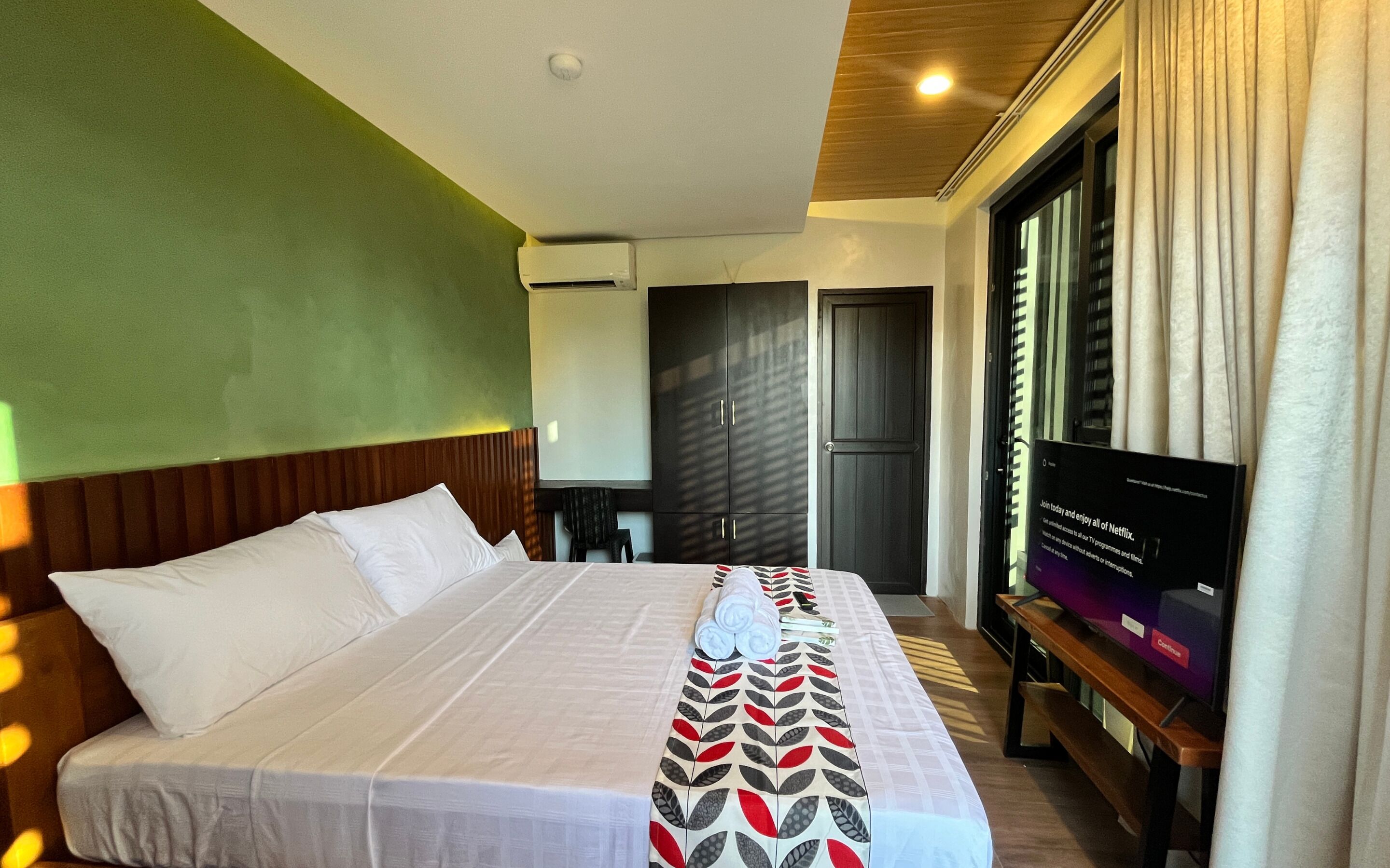 Quarto de hotel com cama, televisão, guarda-roupa e escrivaninha.