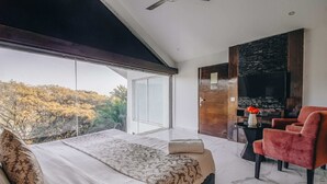 Quarto com cama grande, televisão, cadeira vermelha e vista para árvores.