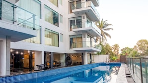 Um hotel moderno com piscina, várias varandas e vista para palmeiras.