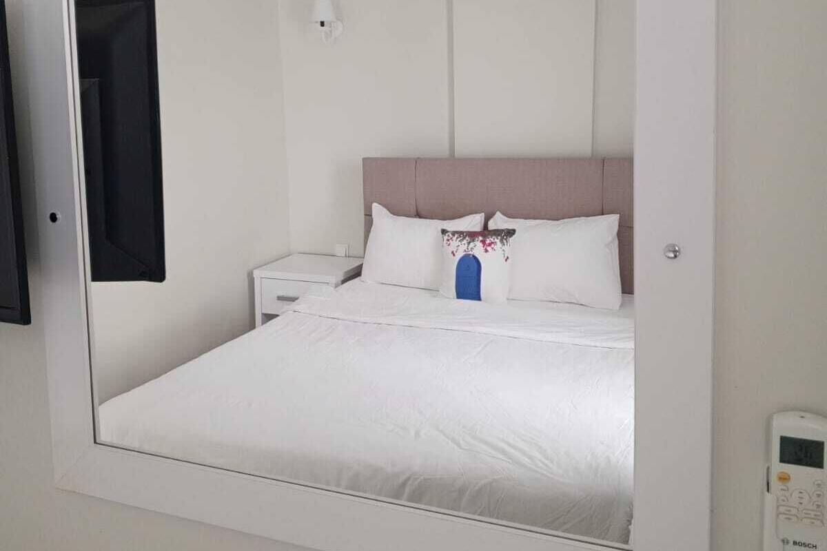 Quarto de hotel com um espelho grande refletindo a cama e uma parede branca.