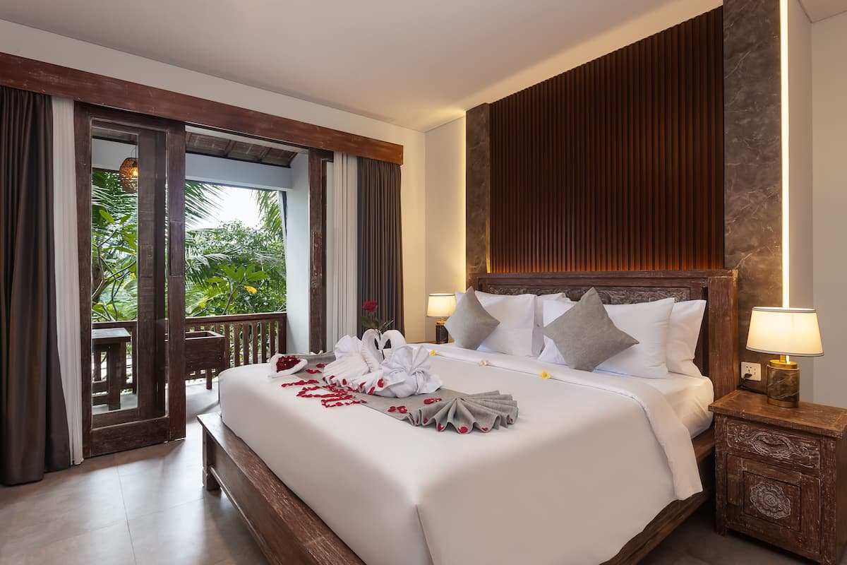 Quarto de hotel com uma cama grande, cabeceira de madeira e varanda com vista para o verde.