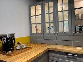 Cozinha com armários cinza, bancada de madeira, máquina de café preta e um relógio.