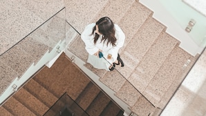 Uma pessoa descendo uma escadaria em um edifício moderno, com corrimãos de vidro e piso de terrazzo.