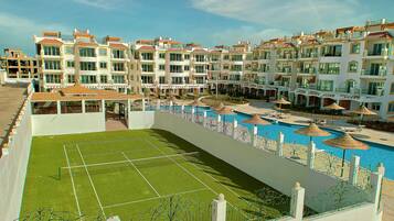 Hotel com várias varandas, piscina e quadra de tênis.
