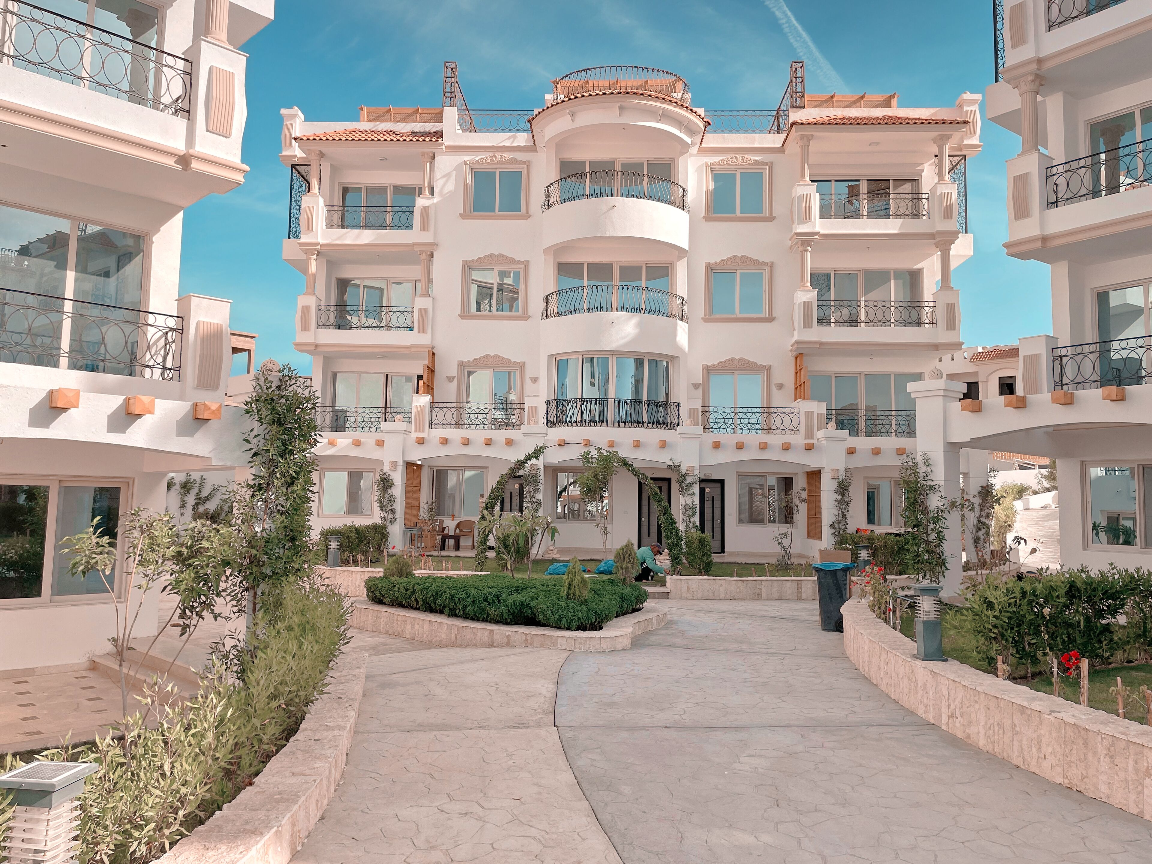 Um edifício residencial de vários andares, com varandas, um pátio central e um jardim bem cuidado.