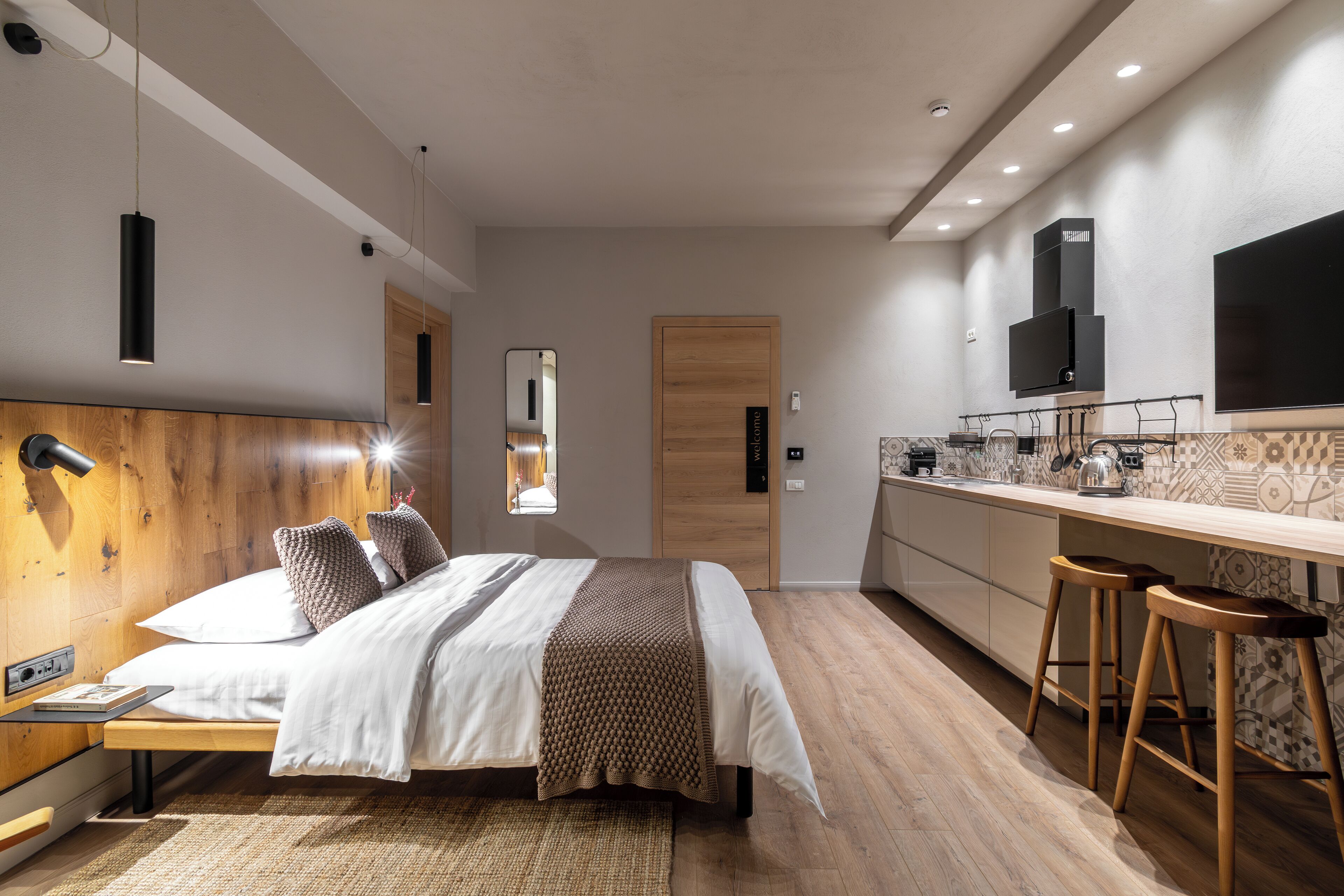 Quarto moderno com cabeceira de madeira, cama grande, mesas de cabeceira, espelho e televisão embutida.