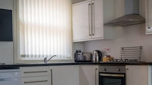 Uma cozinha moderna com armários brancos, forno embutido, fogão a gás e janela com persianas.