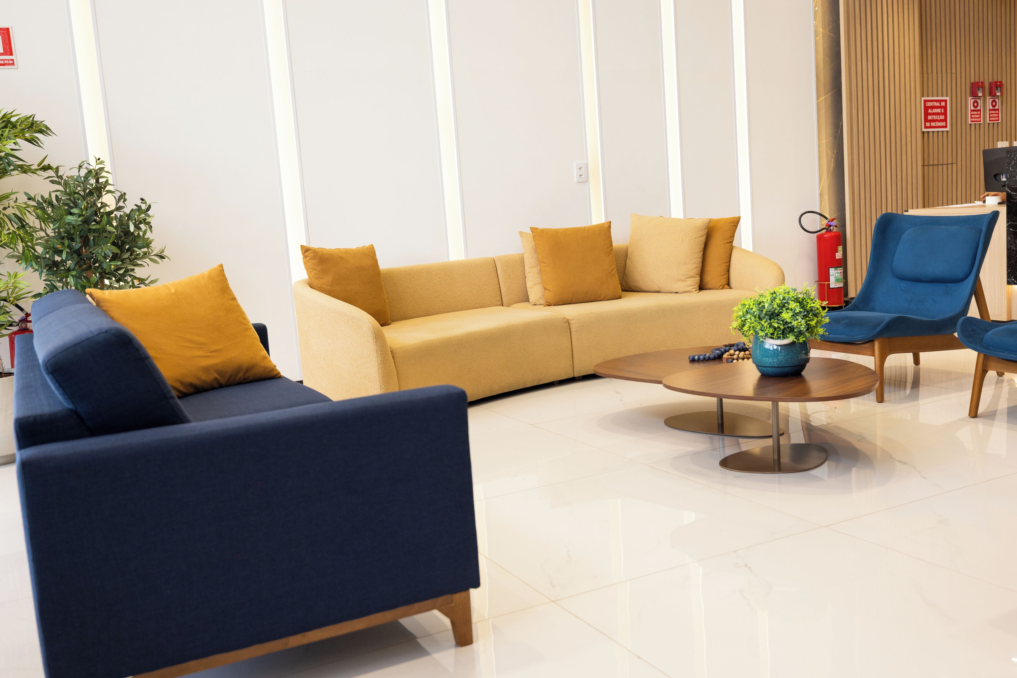 Um hall de hotel moderno com sofá, poltrona e uma mesa redonda com uma planta.
