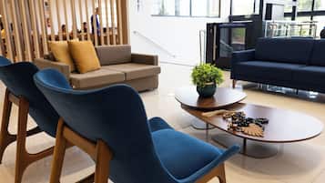 Um hall de hotel moderno com área de estar, com cadeiras azuis, um sofá cinza e um painel de madeira.