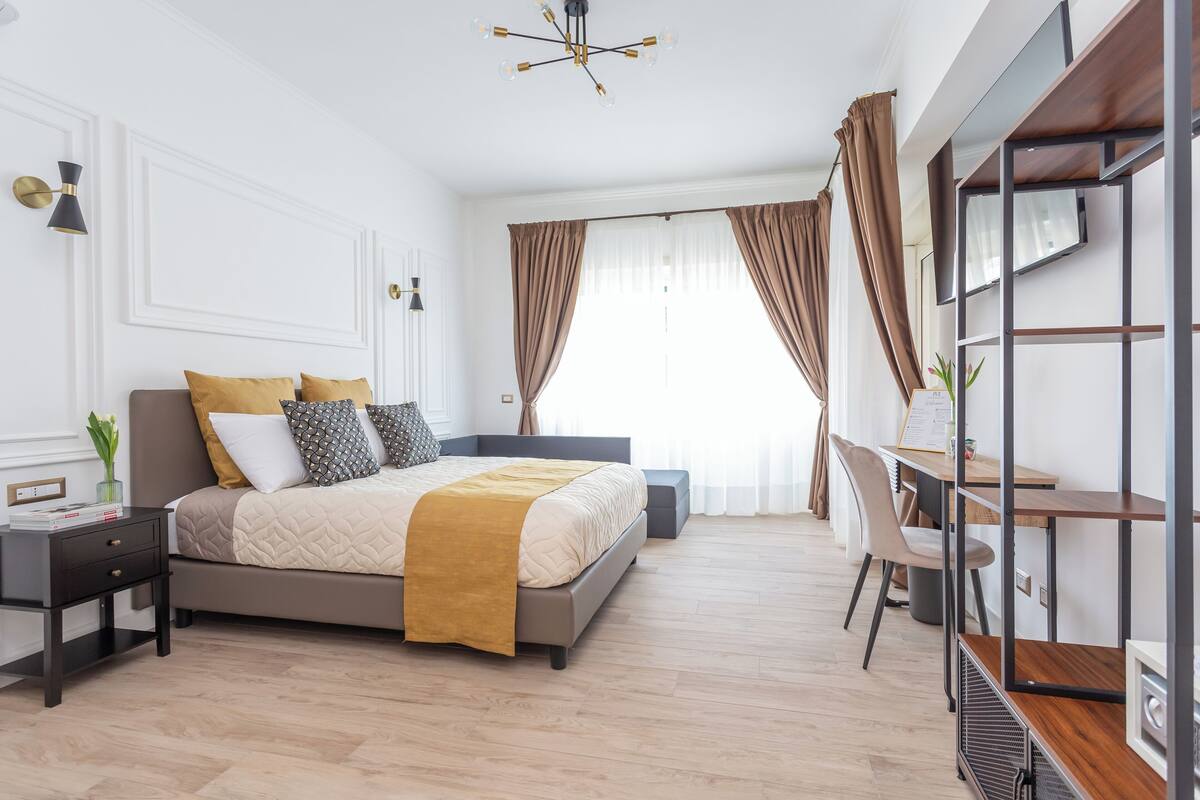 Quarto moderno com cama, mesas de cabeceira, escrivaninha e uma cadeira.
