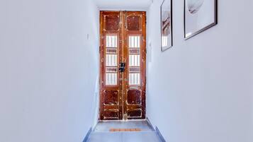 Um corredor com porta de madeira, chão de azulejos e quadros nas paredes.