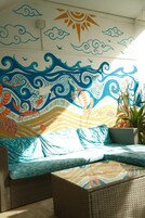 Um quarto com uma cama, um sofá e uma tapeçaria de parede retratando uma cena tropical.