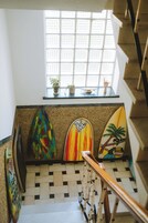 Uma escadaria com corrimão, uma janela com vista para o exterior e três pranchas de surf encostadas na parede.