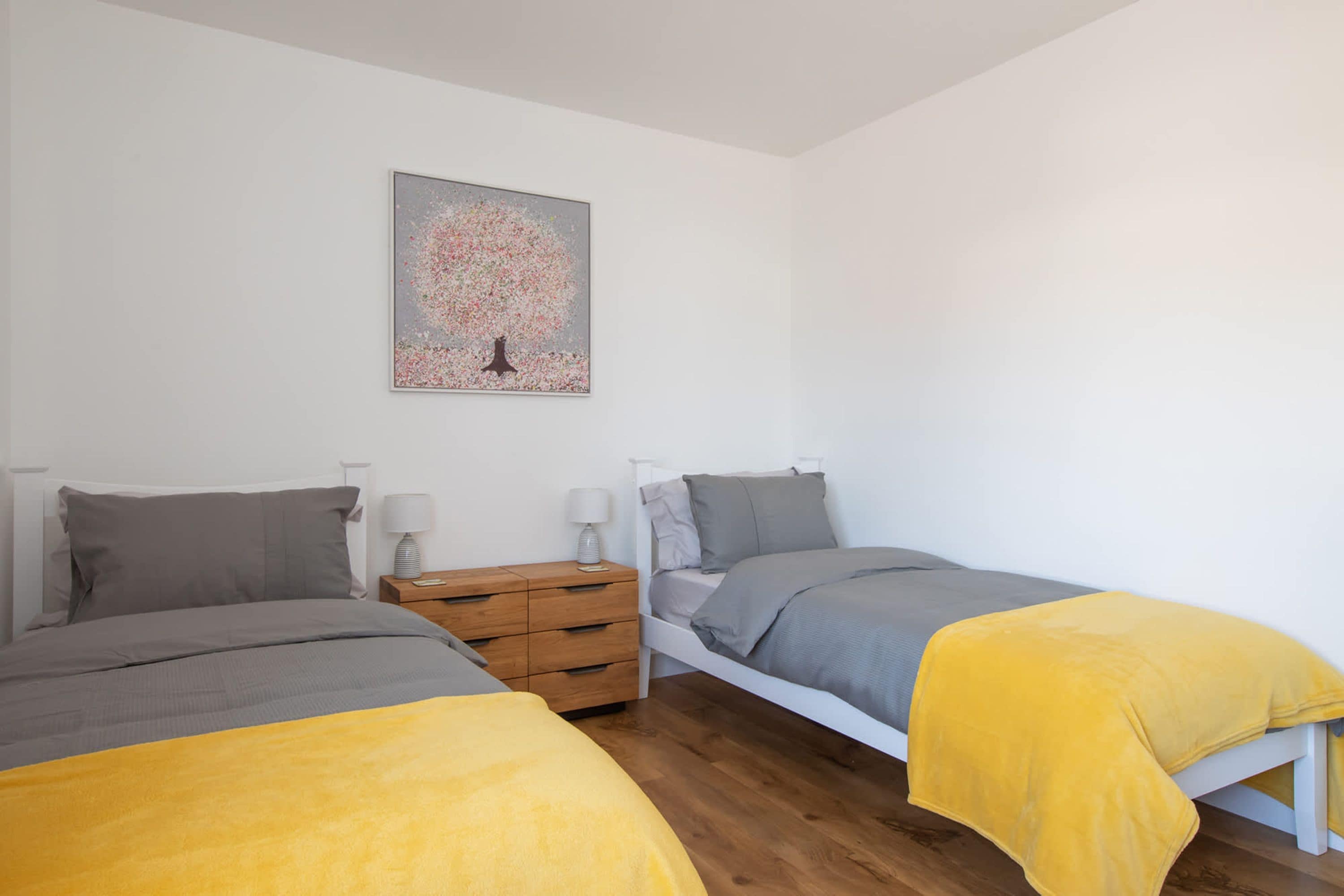 Quarto com duas camas, mesa de cabeceira de madeira e um quadro pendurado na parede.