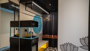 Quarto de hotel moderno com piso xadrez preto e branco, minibar azul e preto, um cabide de madeira e uma grande peça decorativa na parede.