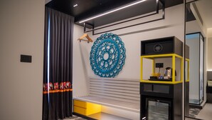 Um banheiro moderno com um banco, um objeto decorativo na parede, uma prateleira amarela e um espelho.