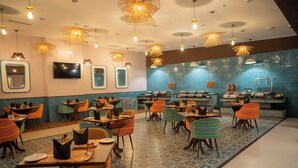 Um restaurante com várias mesas e cadeiras, um balcão com alimentos e uma televisão na parede.