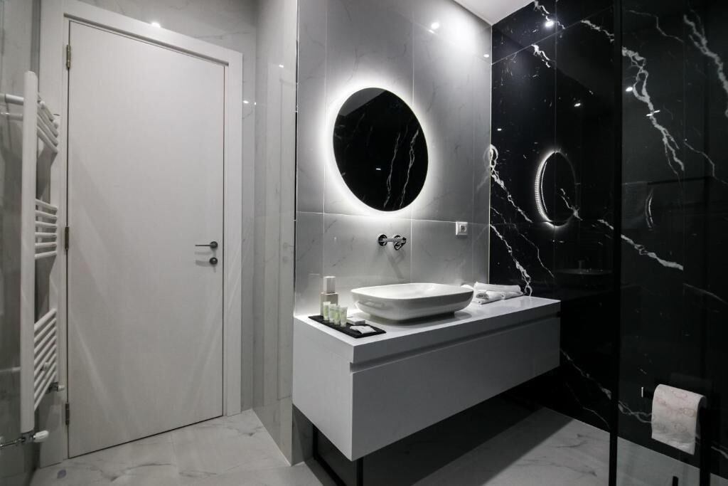 Uma casa de banho moderna com uma toucador branca, um espelho grande com moldura circular e uma parede de mármore preto.