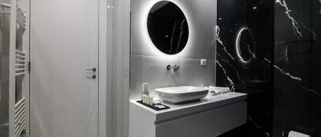 Uma casa de banho moderna com uma toucador branca, um espelho grande com moldura circular e uma parede de mármore preto.