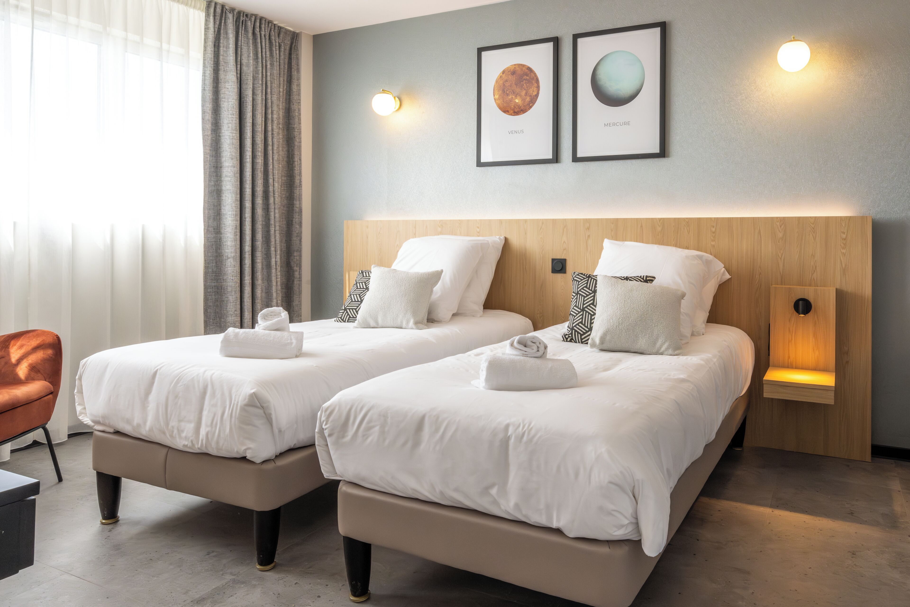 Quarto de hotel com duas camas, cabeceira de madeira e luminárias fixadas na parede.