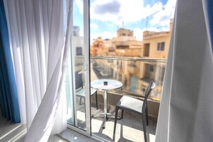 Varanda com porta de vidro, uma mesa redonda pequena e uma cadeira, com vista para a paisagem urbana.