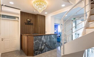Bancada de recepção com painel de madeira e detalhes em mármore, um candelabro e uma escada em espiral.