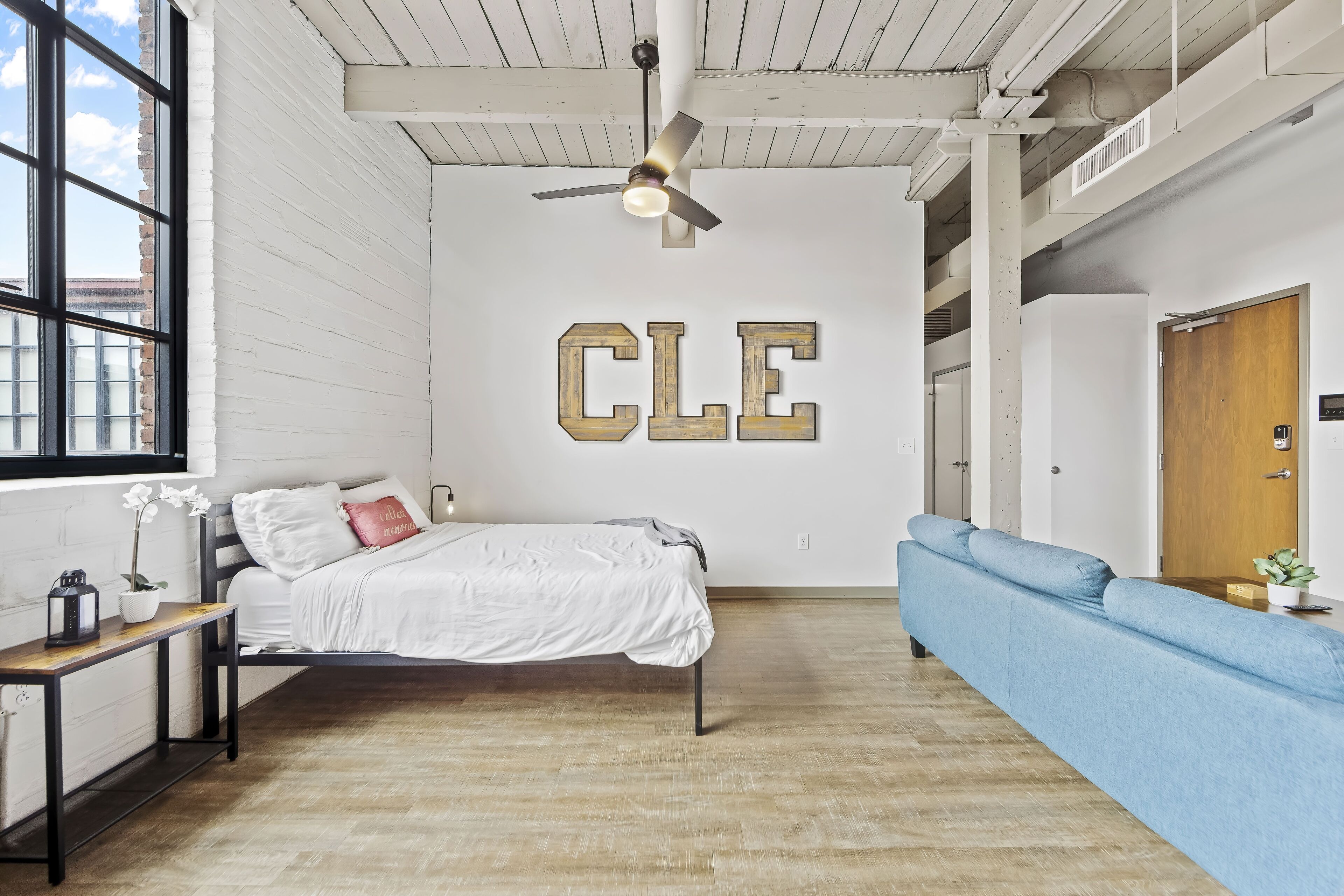 Quarto com cama, sofá azul, ventoinha no teto e parede com as letras "CLE".