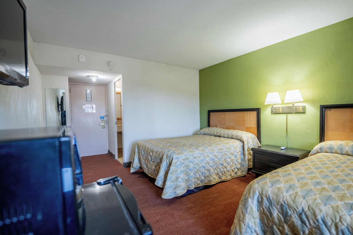 Quarto de hotel com duas camas, uma mesa, uma televisão e uma parede verde.