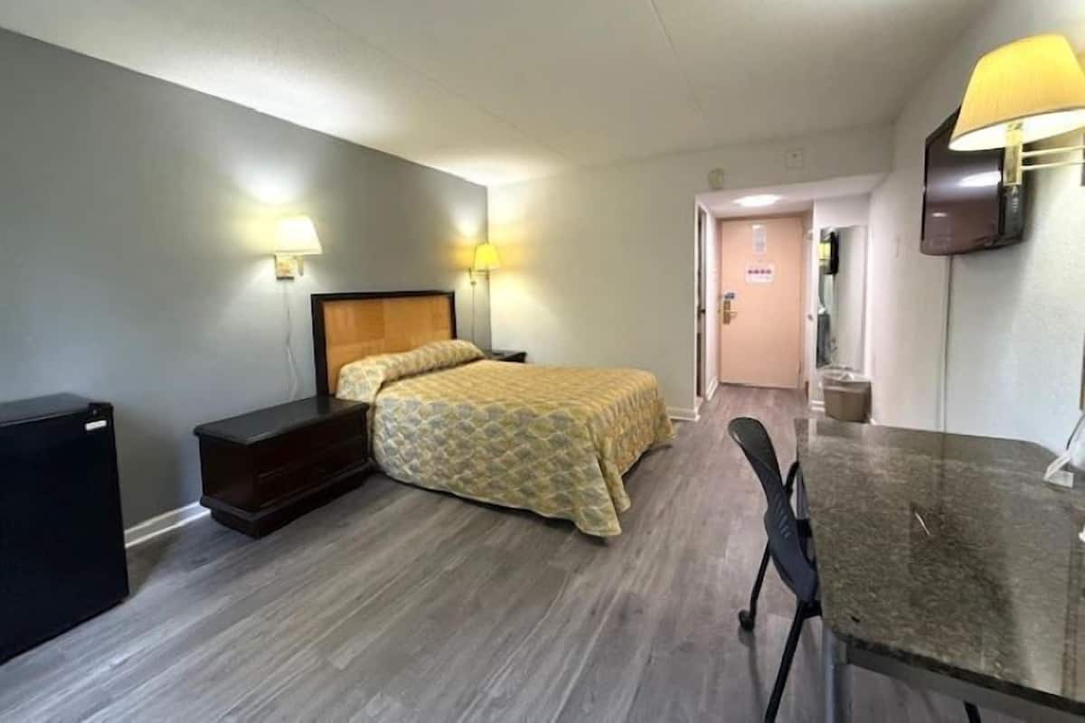 Quarto de hotel com cama, mesas de cabeceira, escrivaninha e uma cadeira. Há uma porta que dá para um banheiro.