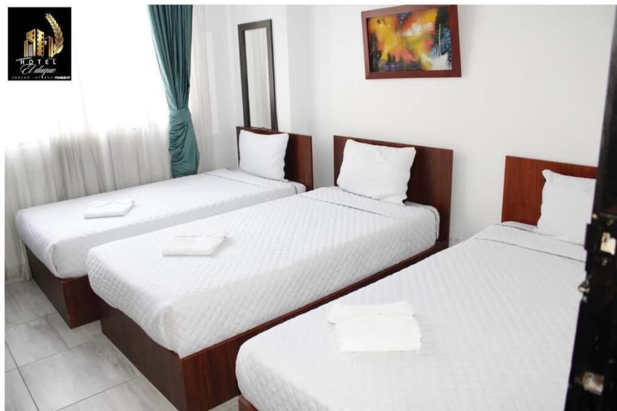 Quarto de hotel com três camas de solteiro, roupa de cama branca, um espelho grande e um quadro colorido na parede.