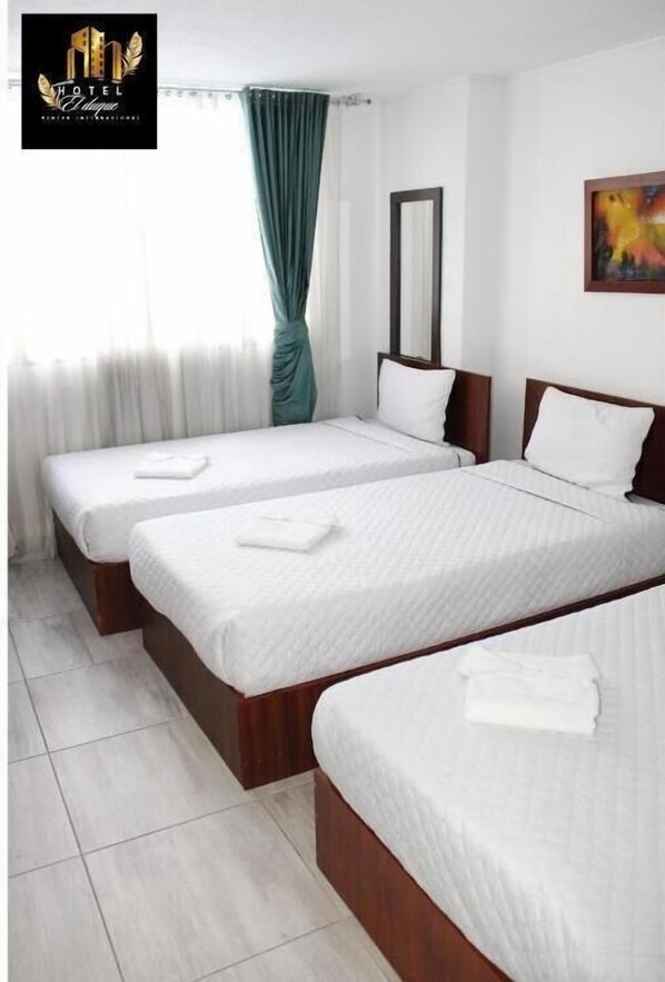Quarto de hotel com duas camas de solteiro, uma janela grande com cortinas translúcidas, um espelho e um quadro na parede.