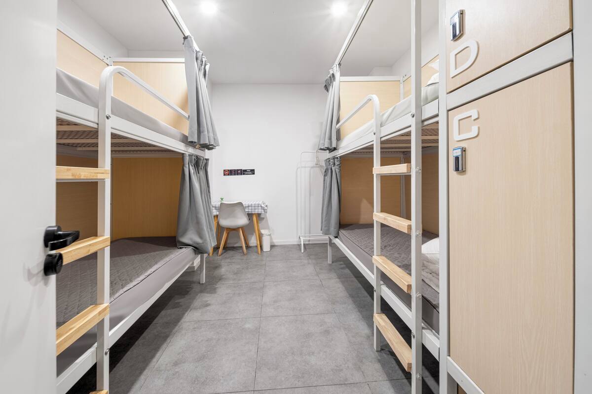 Um quarto em dormitório com beliches, uma escrivaninha e uma cadeira.