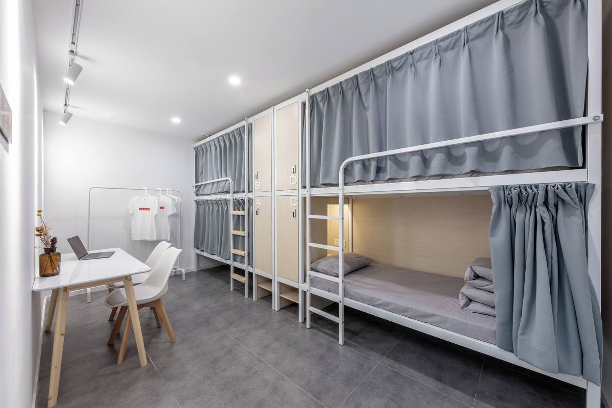 Um quarto de estudante com beliches, escrivaninha, cadeiras e armário.