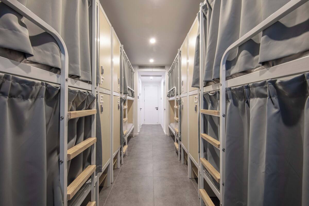 Um corredor com beliches dispostos em ambos os lados, conduzindo a uma porta no final.