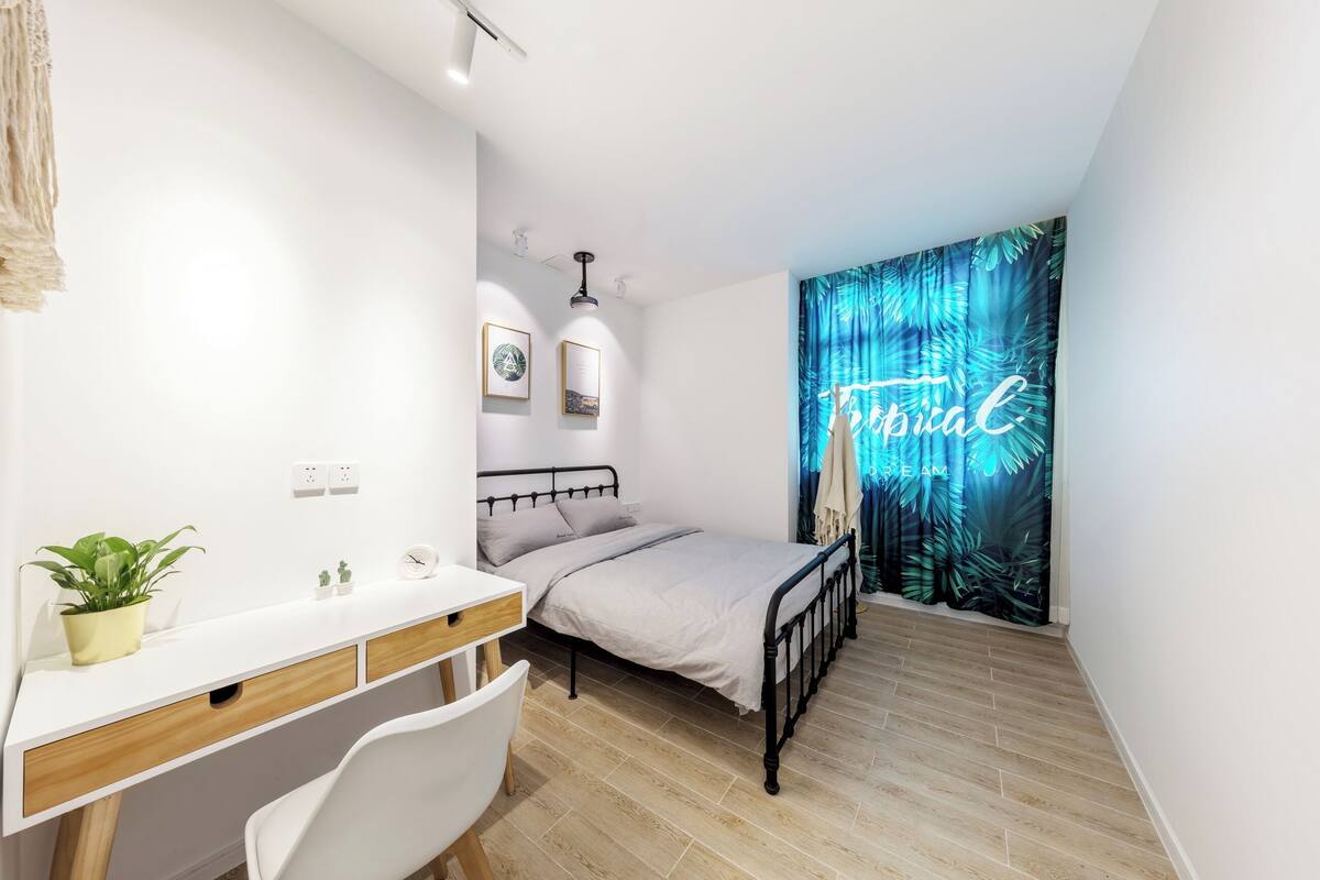 Quarto com cama, mesa de cabeceira, cadeira e escrivaninha com uma planta.