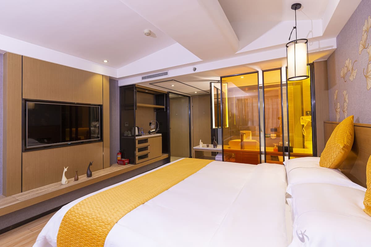 Quarto de hotel moderno com uma cama grande, televisão, closet espaçoso e banheiro com chuveiro de vidro.