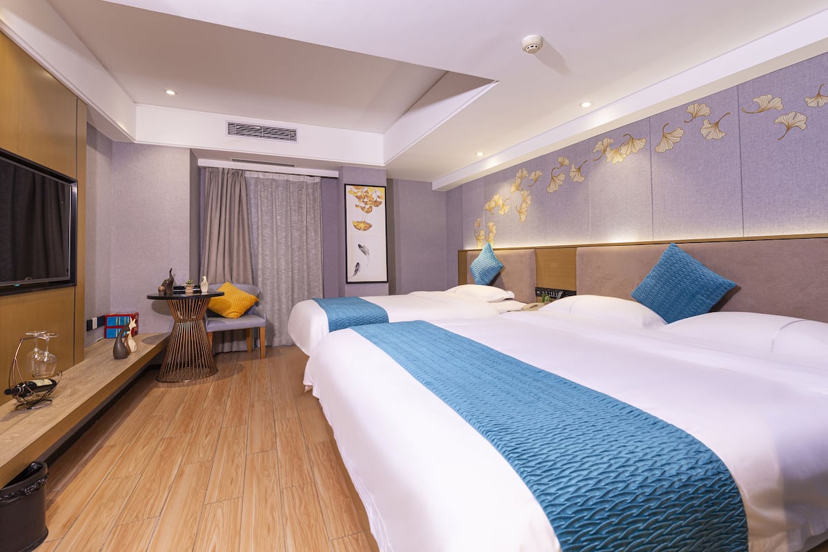 Quarto de hotel com duas camas, uma mesa pequena, uma cadeira e uma televisão.