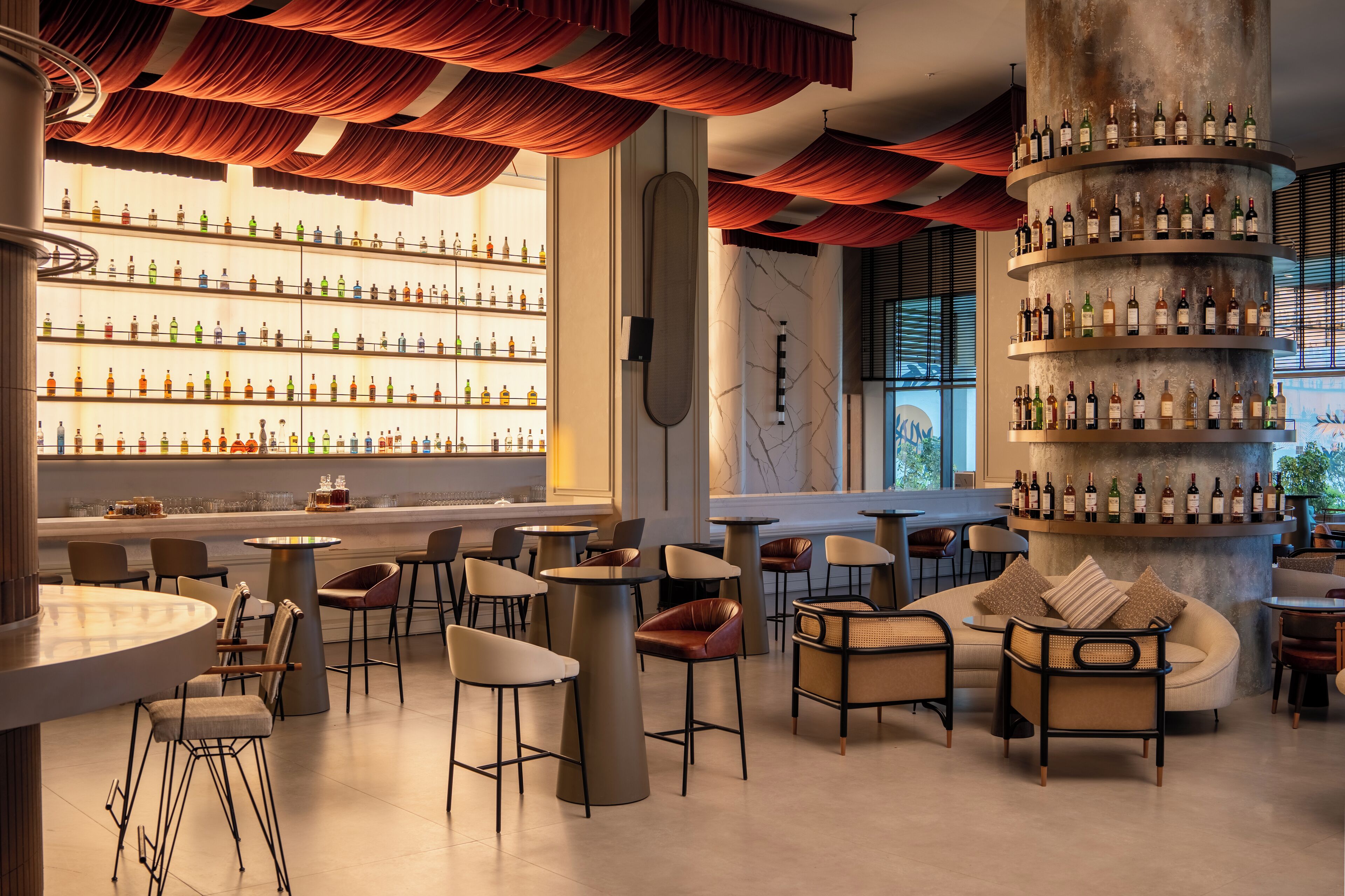 Uma área de bar moderna com várias opções de assento, um display de vinhos e uma coluna central imponente.