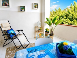 Uma varanda com uma cadeira, uma mesa com toalha de mesa azul e plantas em vasos.