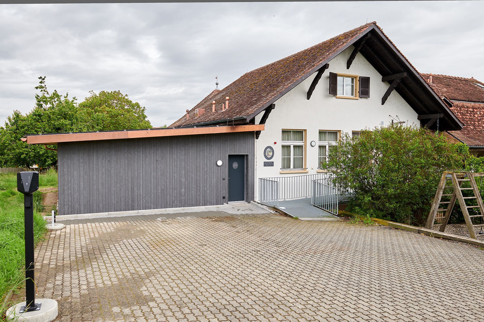 Uma casa de dois andares com telhado inclinado, garagem e entrada pavimentada.