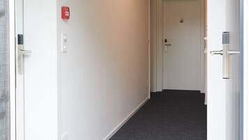 Um corredor com paredes brancas, carpete cinzento e uma porta no final.