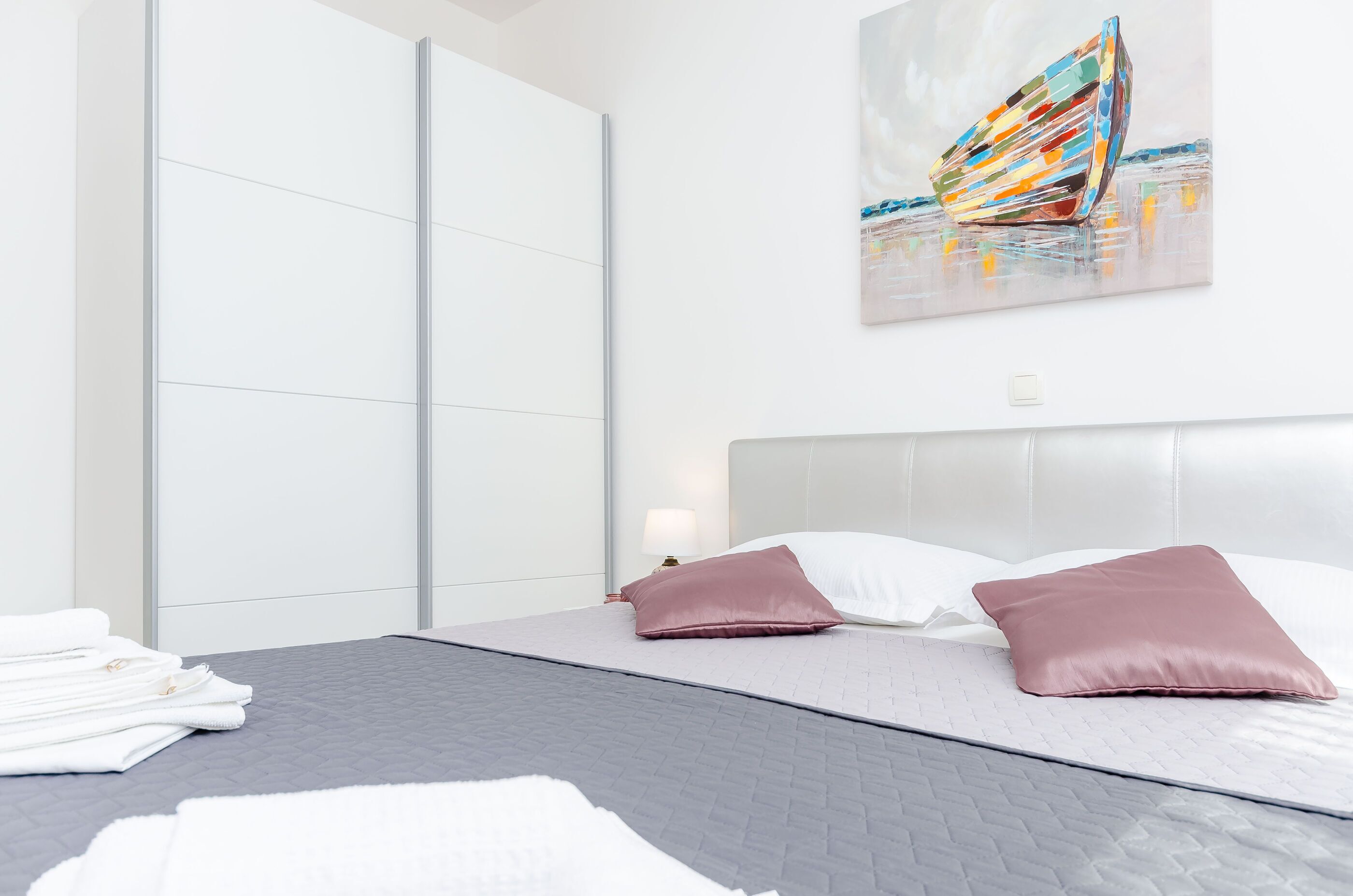 Quarto de hotel moderno com cama grande, roupa de cama branca e um quadro na parede.