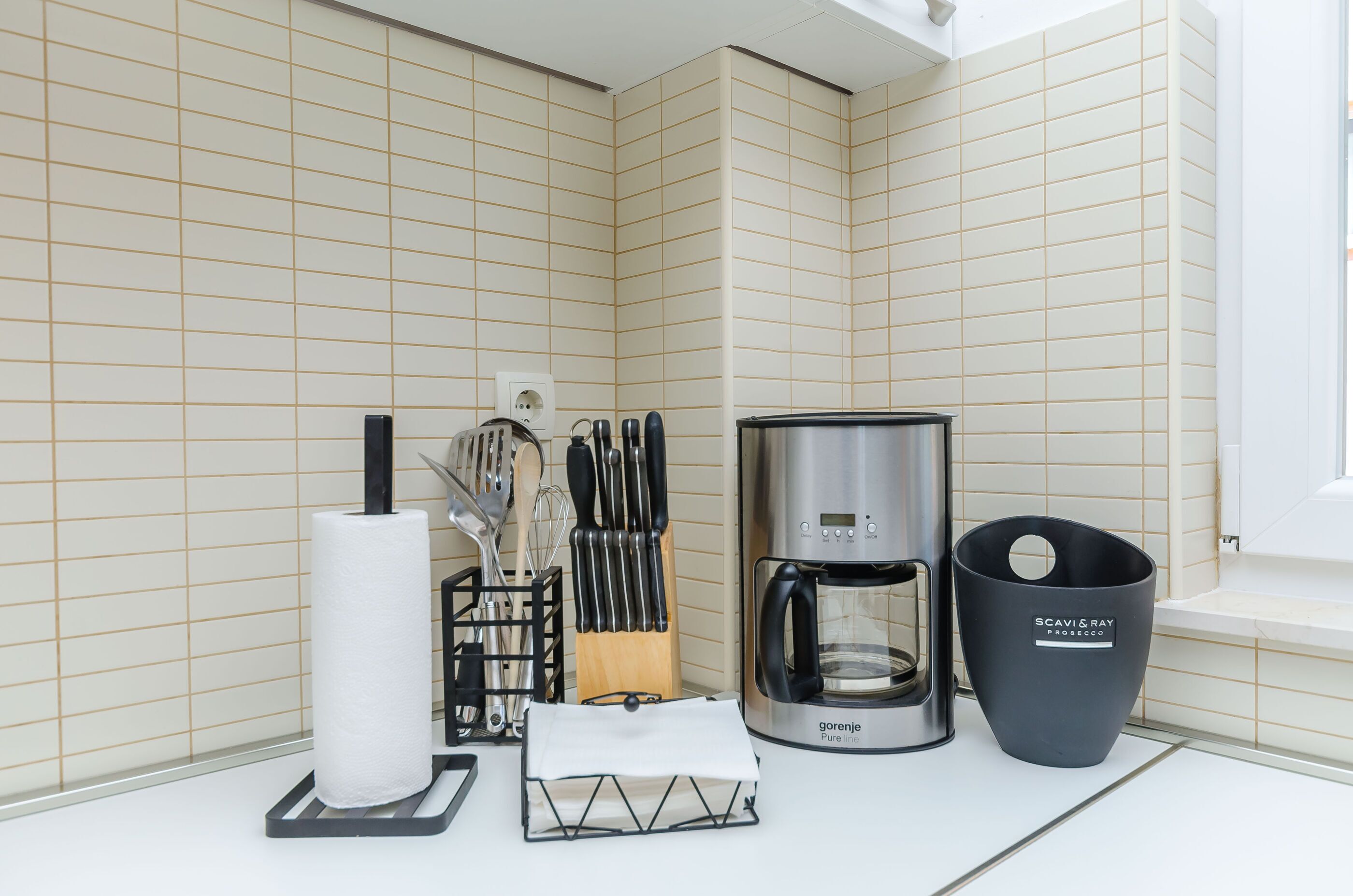 Cozinha com cafeteira, porta-panos, bloco de facas e lixeira.