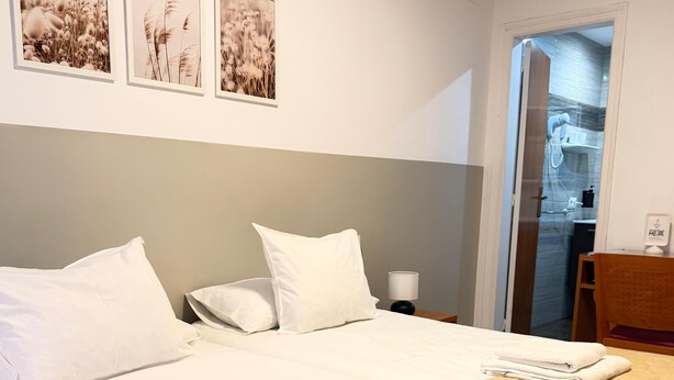 Quarto de hotel com duas camas, roupa de cama branca, um cobertor bege e um conjunto de toalhas.