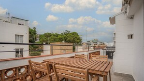 Terraço no telhado com mobiliário de madeira e vista para prédios ao redor.