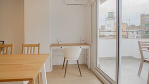 Quarto moderno com escrivaninha de madeira, cadeira branca e ampla janela com vista para a paisagem urbana.