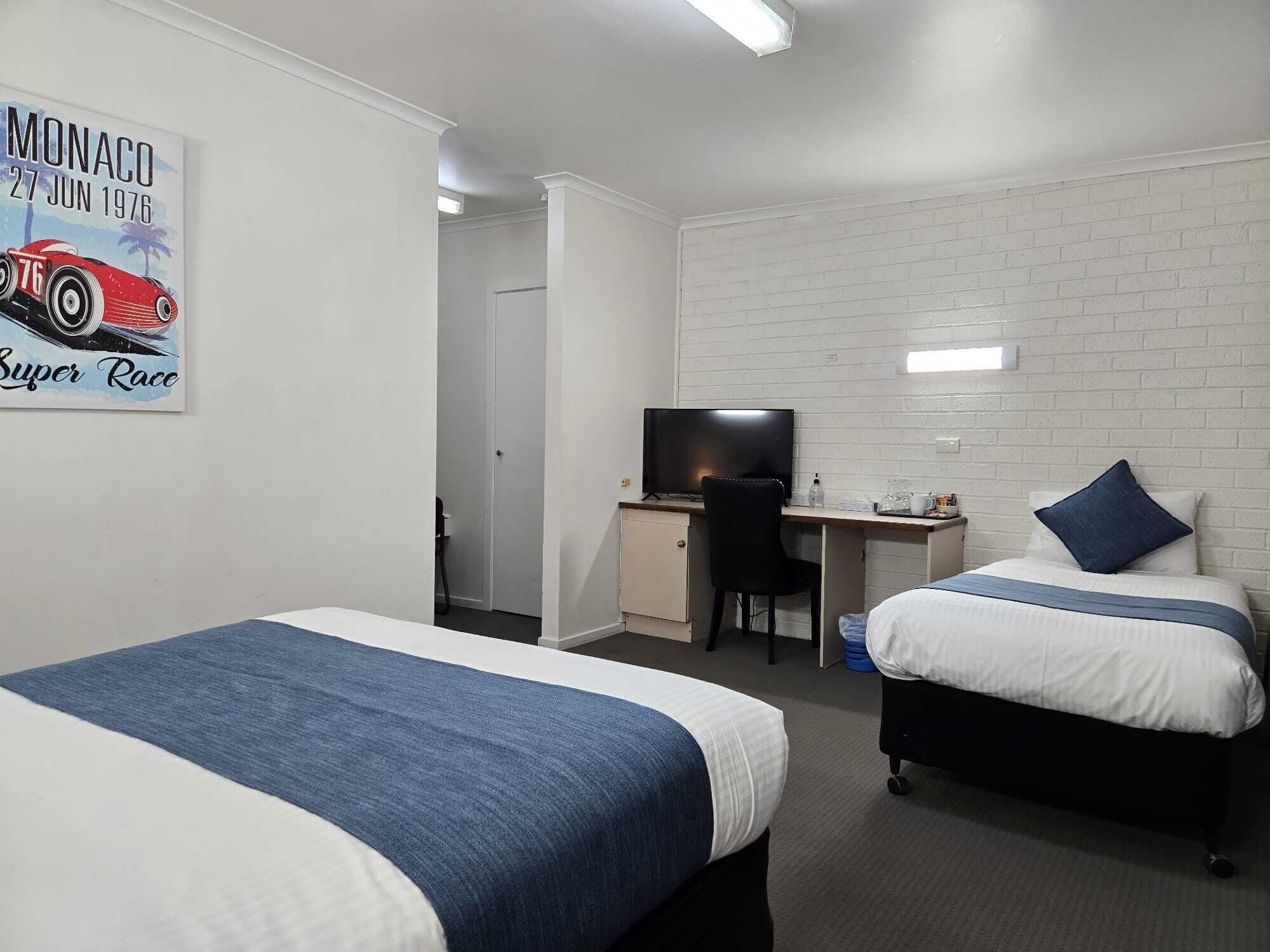 Quarto de hotel com duas camas, uma escrivaninha, uma televisão e um cartaz na parede.