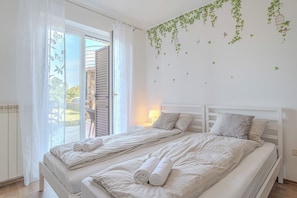 Quarto com cama, cortinas, vista pela janela e parede com decalque de tema natural.
